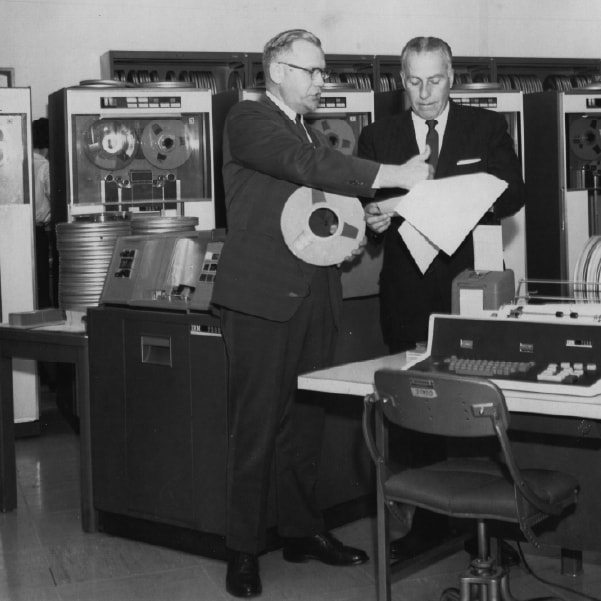 two guys in suits having a conversation in a computer room while one ...