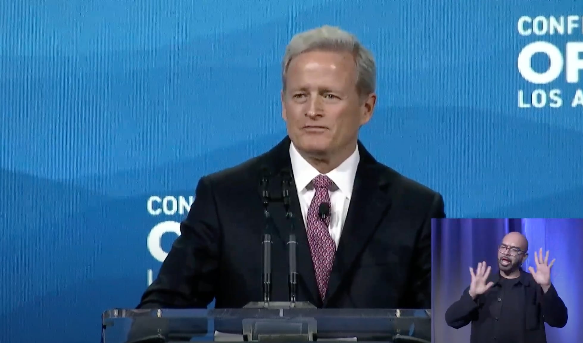 Male in black suit and tie speaking on a podium